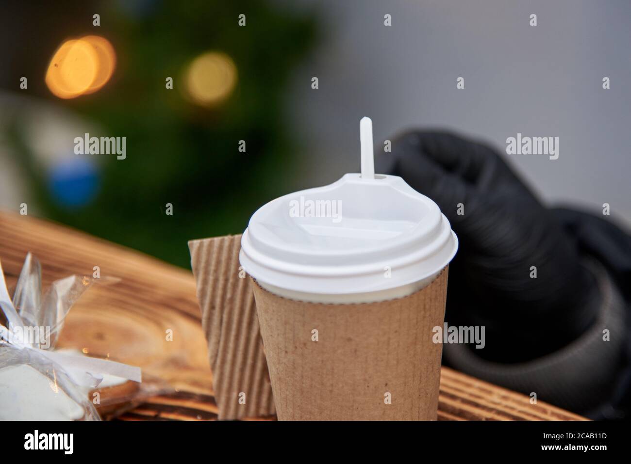Disposable plastic cup in paper packaging with a hot drink on a wooden ...