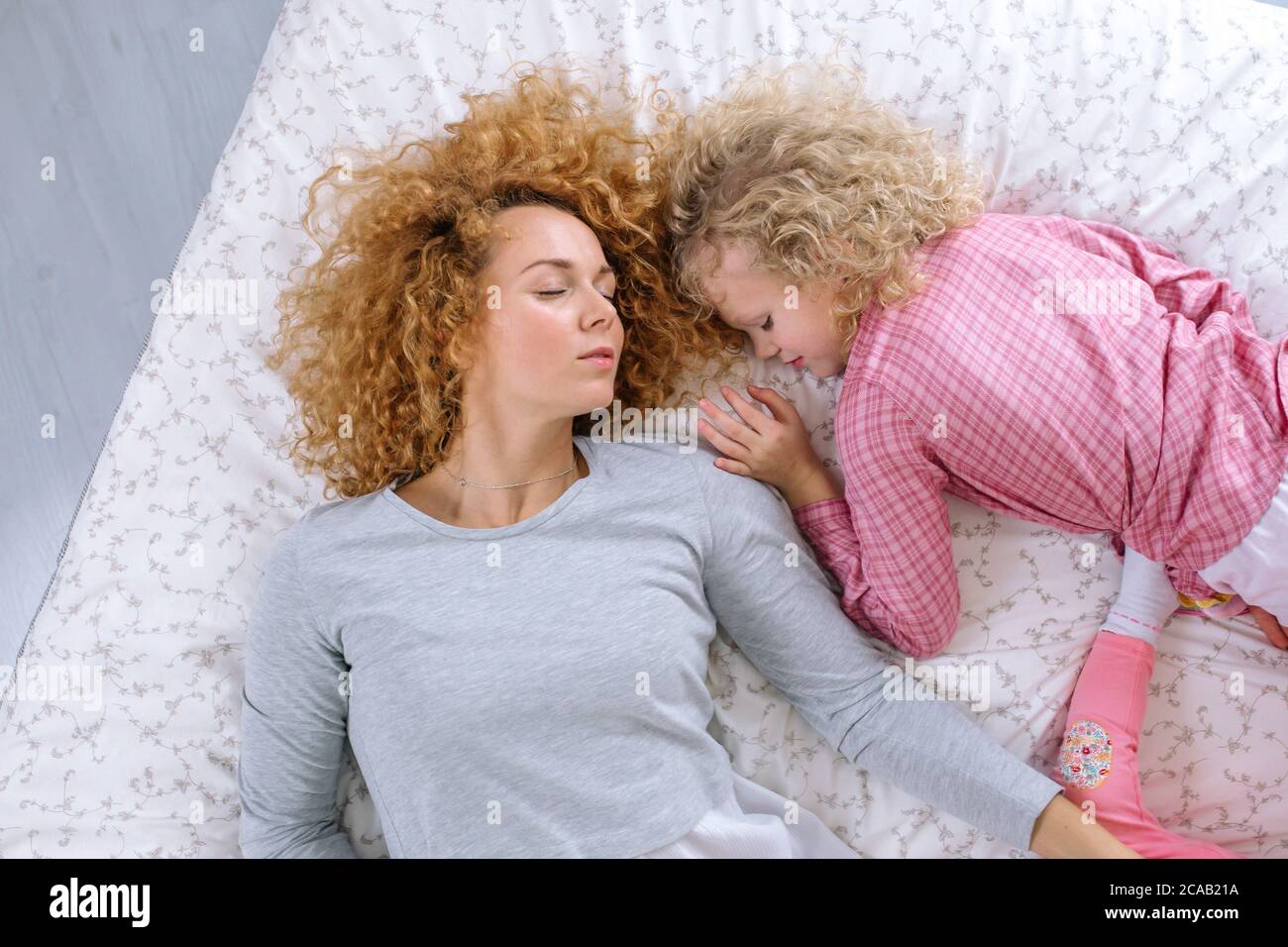 tired ginger woman is sleeping with her adorable daughter. top view ...