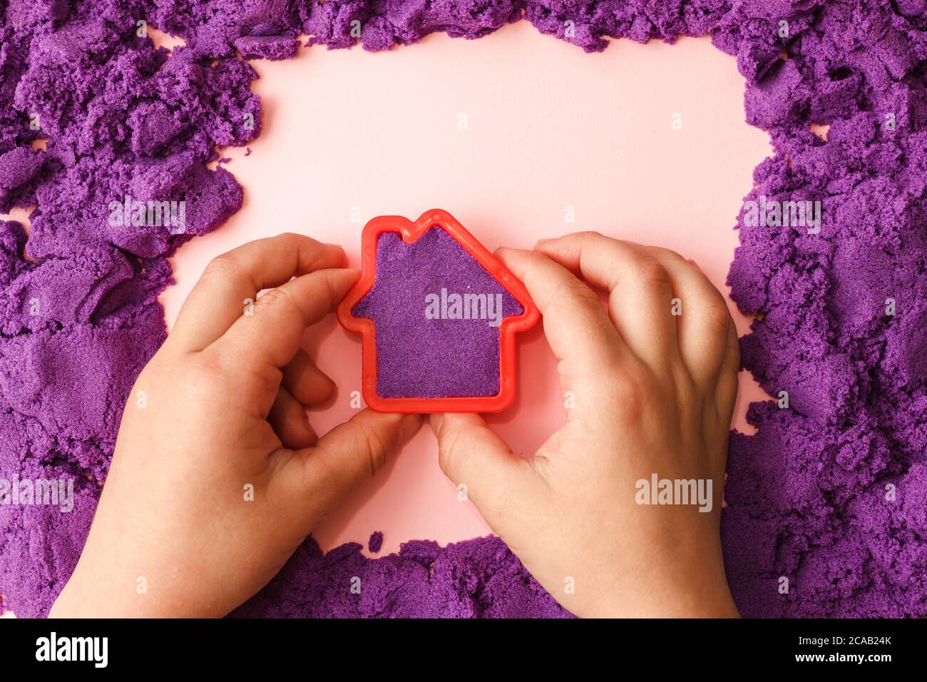 Child playing with violet play sand, kinetic sand and models sand house ...