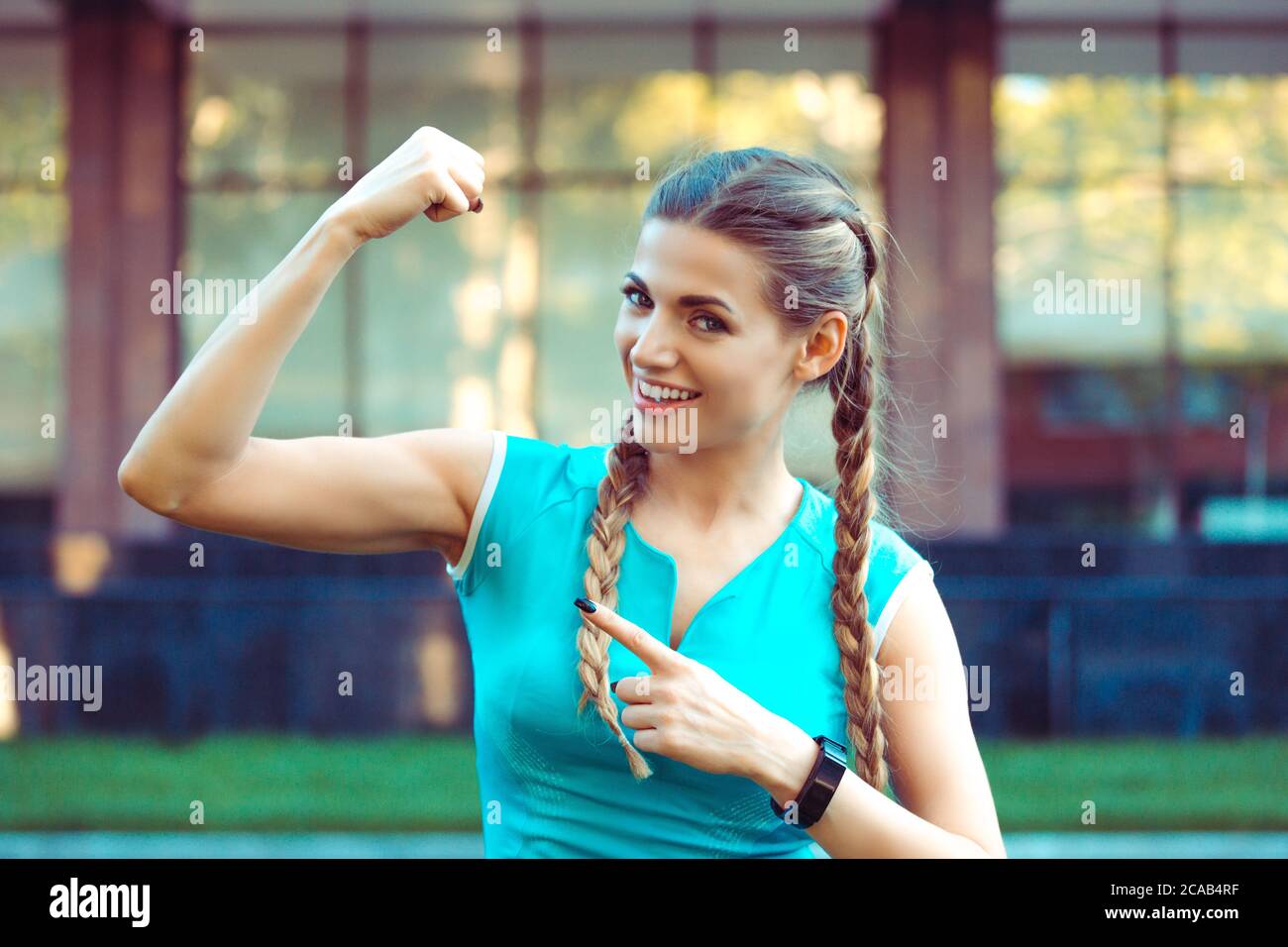 Charming fit sportswoman showing bicep at camera with smile on urban ...