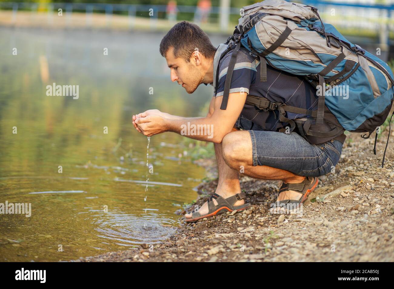 good looking guy is washing his face on the river. thirsty traveler is ...