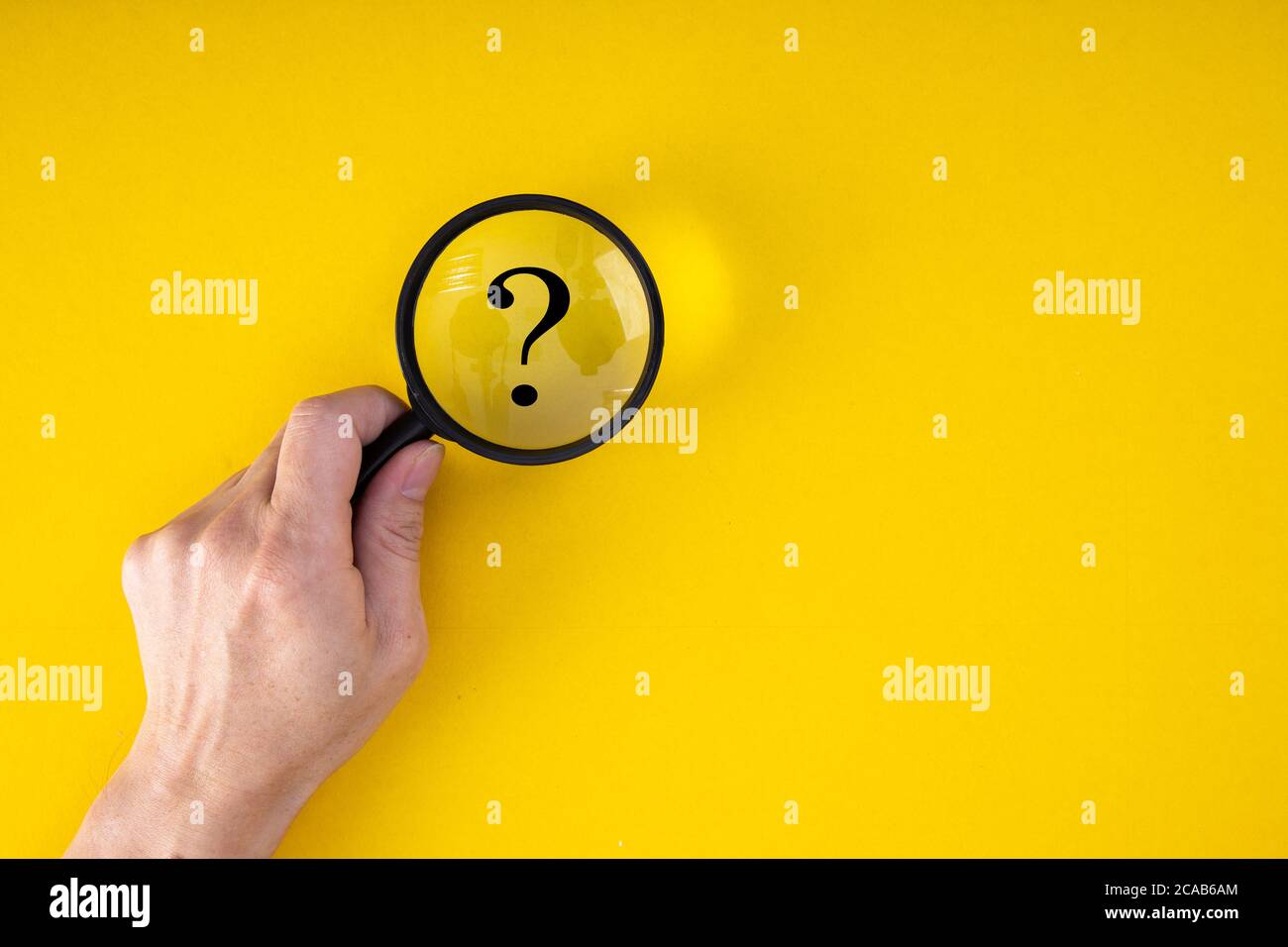 Overhead shot of a hand holding magnifying glass over a question mark ...