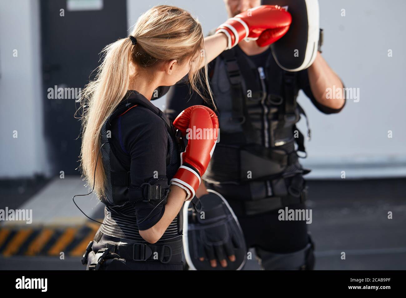sporty girl wearing EMS costume is working out with boxing gloves ...