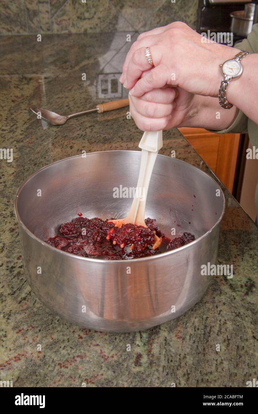 Woman mashing blackberries in preparation for making jam in the kitchen ...