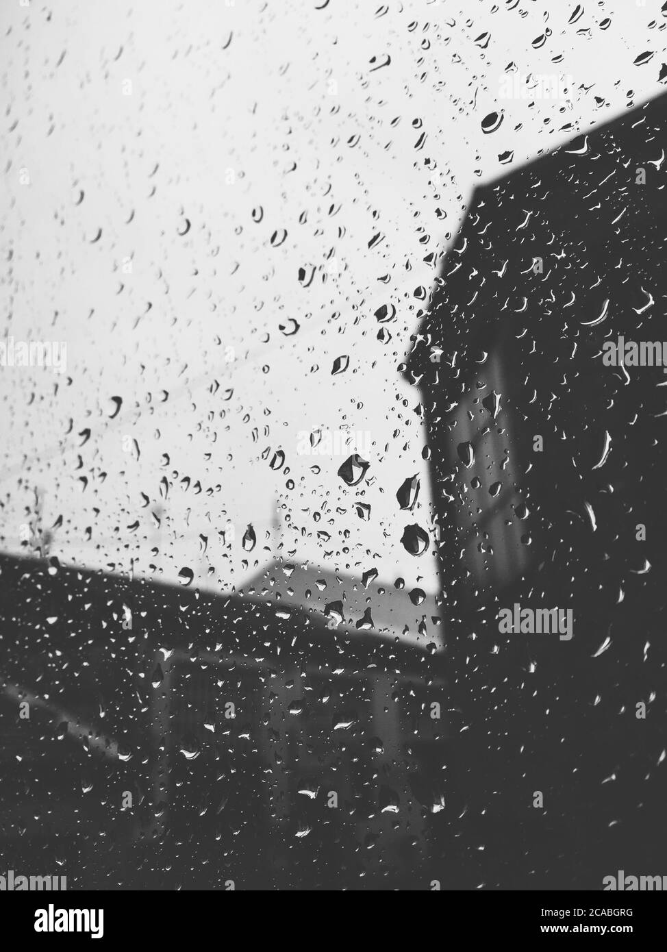 Greyscale closeup shot of raindrops on the window with buildings in the ...