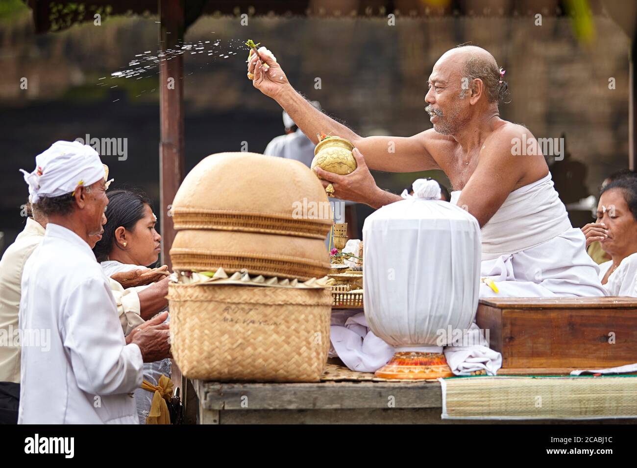 A leader of Balinese Hindu religious ceremonies sprinkling water on ...