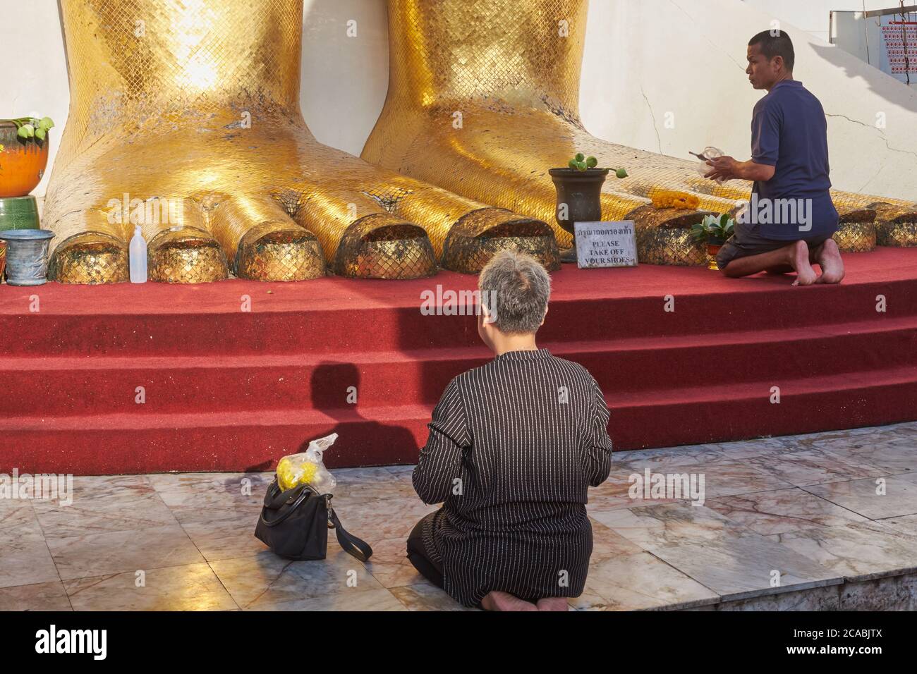 Worshippers sit and pray at the feet of the 32 m high, golden statue of ...