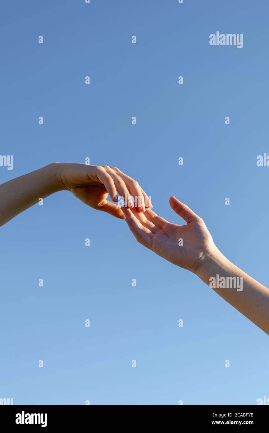 Vertical shot of two hands reaching out to each other on a blue sky ...