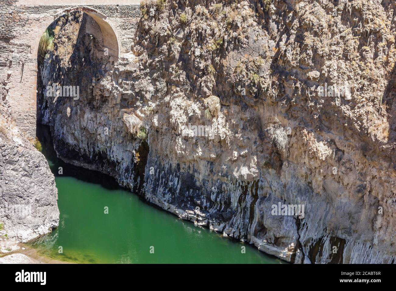 Closeup shot of a cliff and a bridge over green water Stock Photo - Alamy