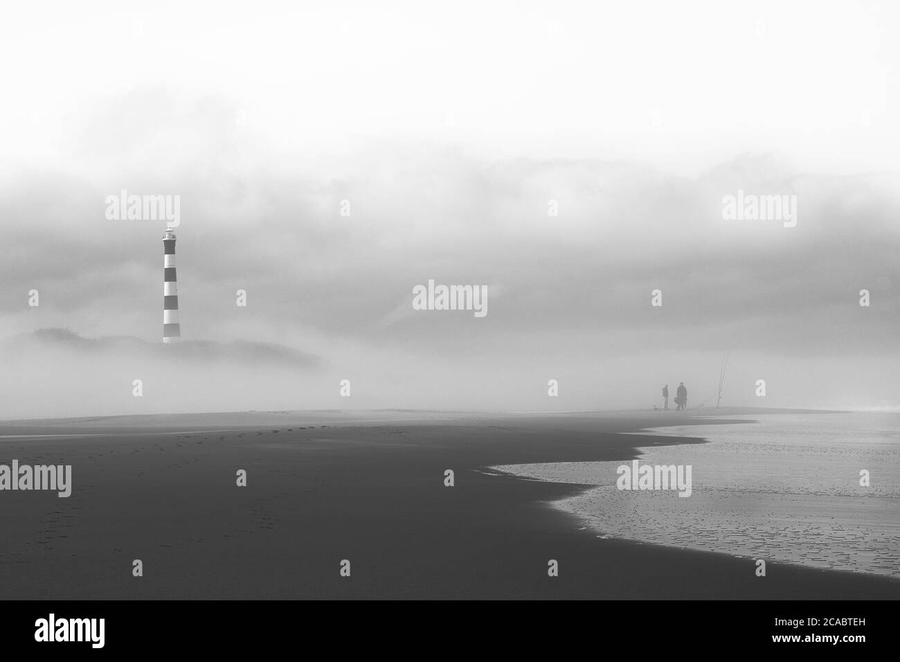 Greyscale shot of a lighthouse visible behind the fog or at the beach ...