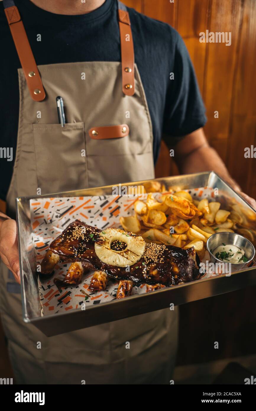 Close-up of a waiter serving delicious barbecued prime rib with french ...
