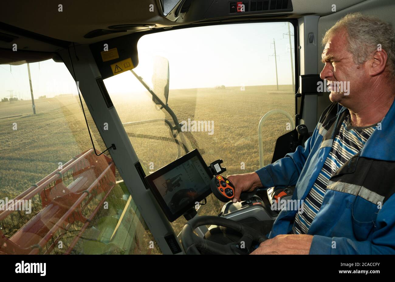 the machine operator at the helm of a modern combine harvester harvests ...