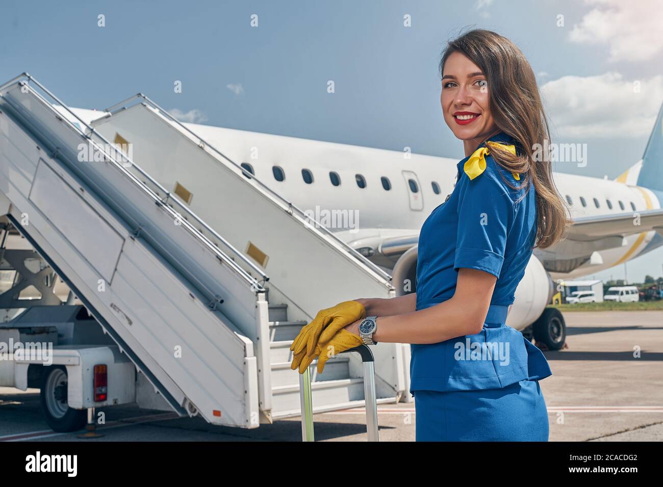 Happy stewardess standing in front of the plane Stock Photo - Alamy