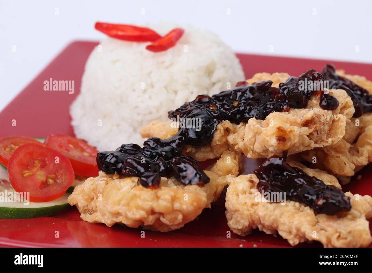 Fried chicken and rice on a red plate with black spicy flavor isolated ...