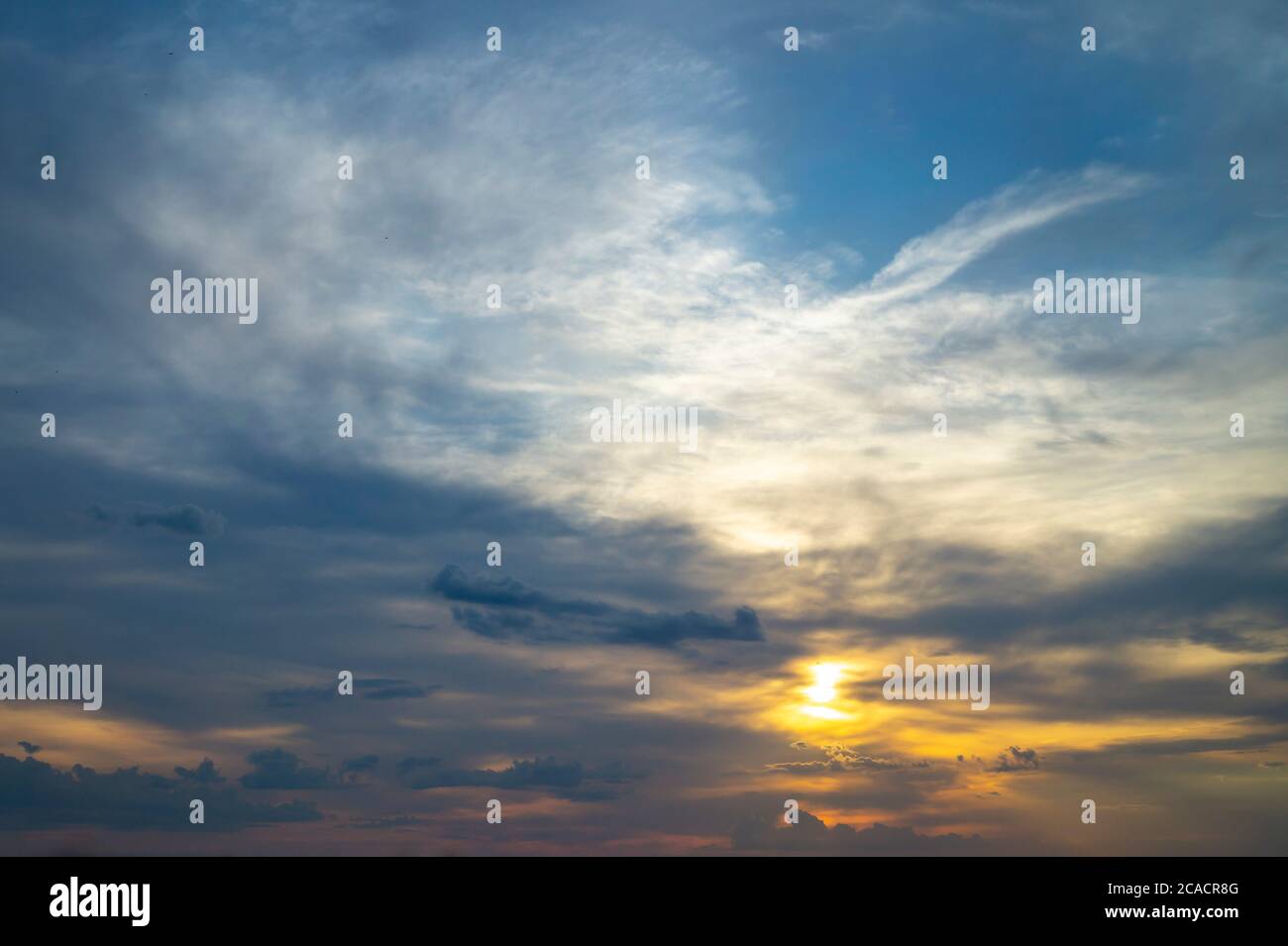 Glowing sun peeking through the clouds at sunset in a twilight blue sky ...