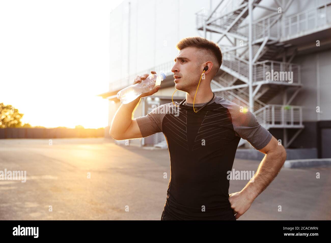 Image of young athletic sportsman in earphones drinking water while ...