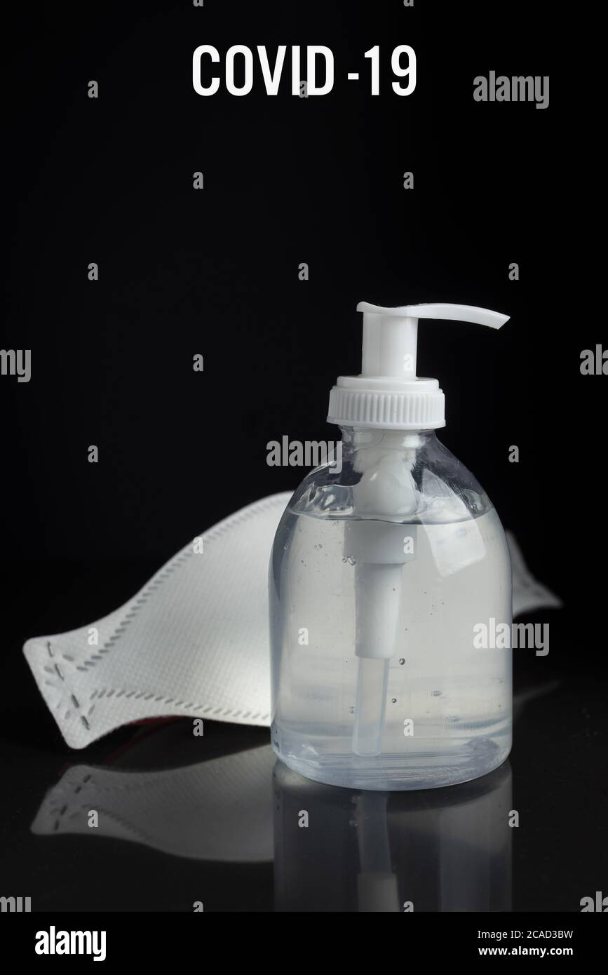Vertical shot of a face mask and hand sanitizer on a black background ...