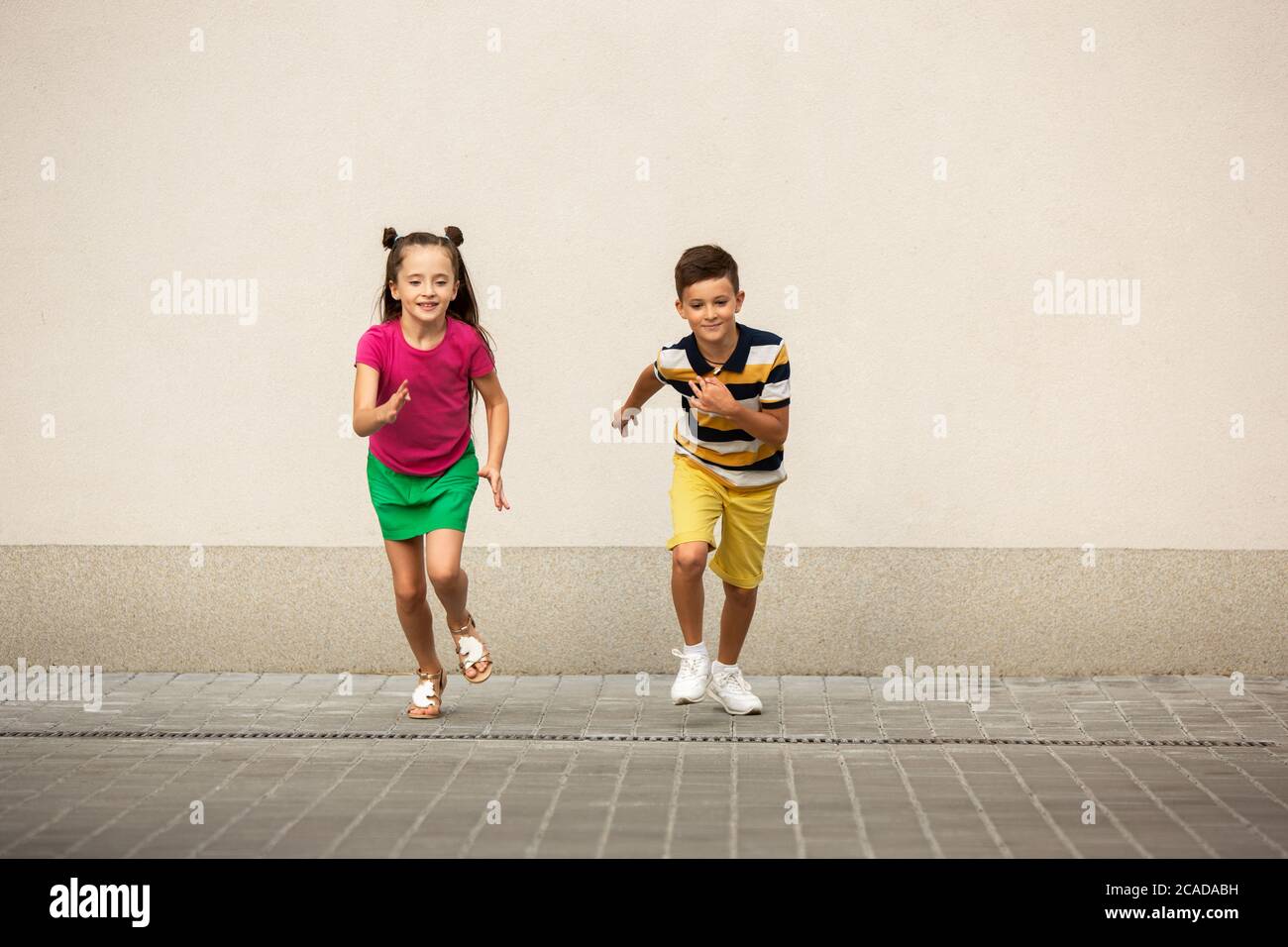 Two smiling kids, boy and girl running together in town, city in summer ...