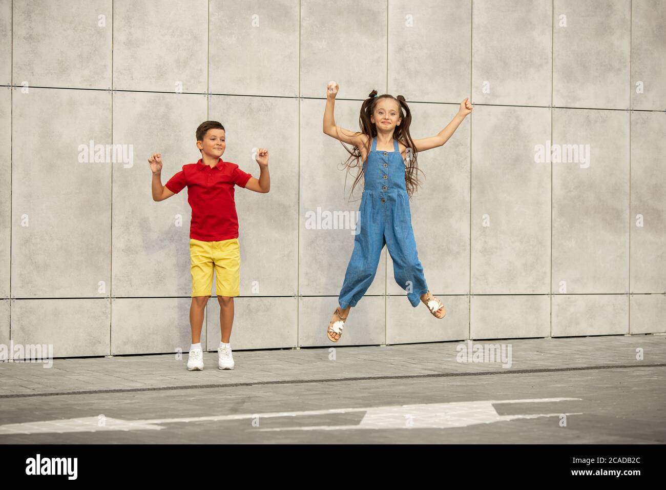 Two smiling kids, boy and girl jumping together in town, city in summer ...