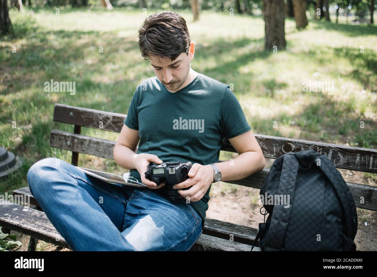 Man sitting on bench in park and looking at his camera Stock Photo - Alamy
