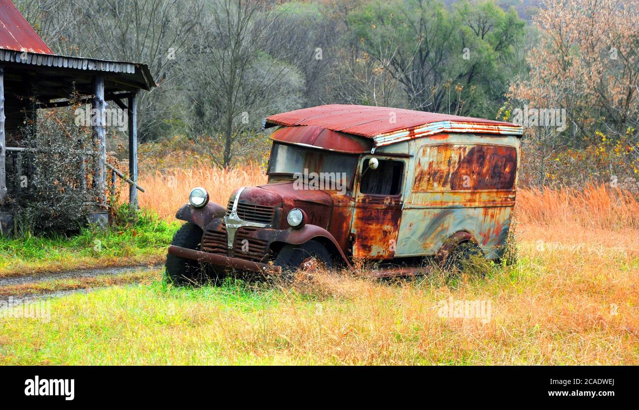 Old Ford delivery truck rusts in front of an log cabin. Green has faded ...