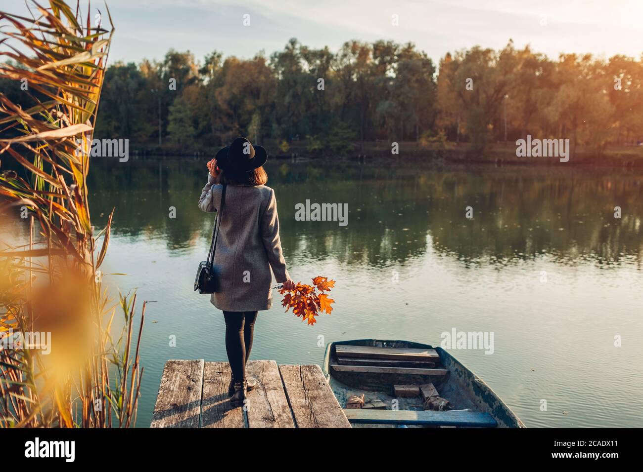 Woman walking on lake pier by boat admiring autumn landscape. Fall ...