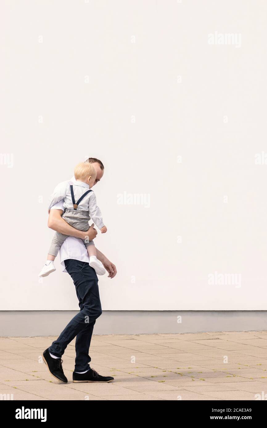 Father and son concept. Father carries child in his hands in white wall ...