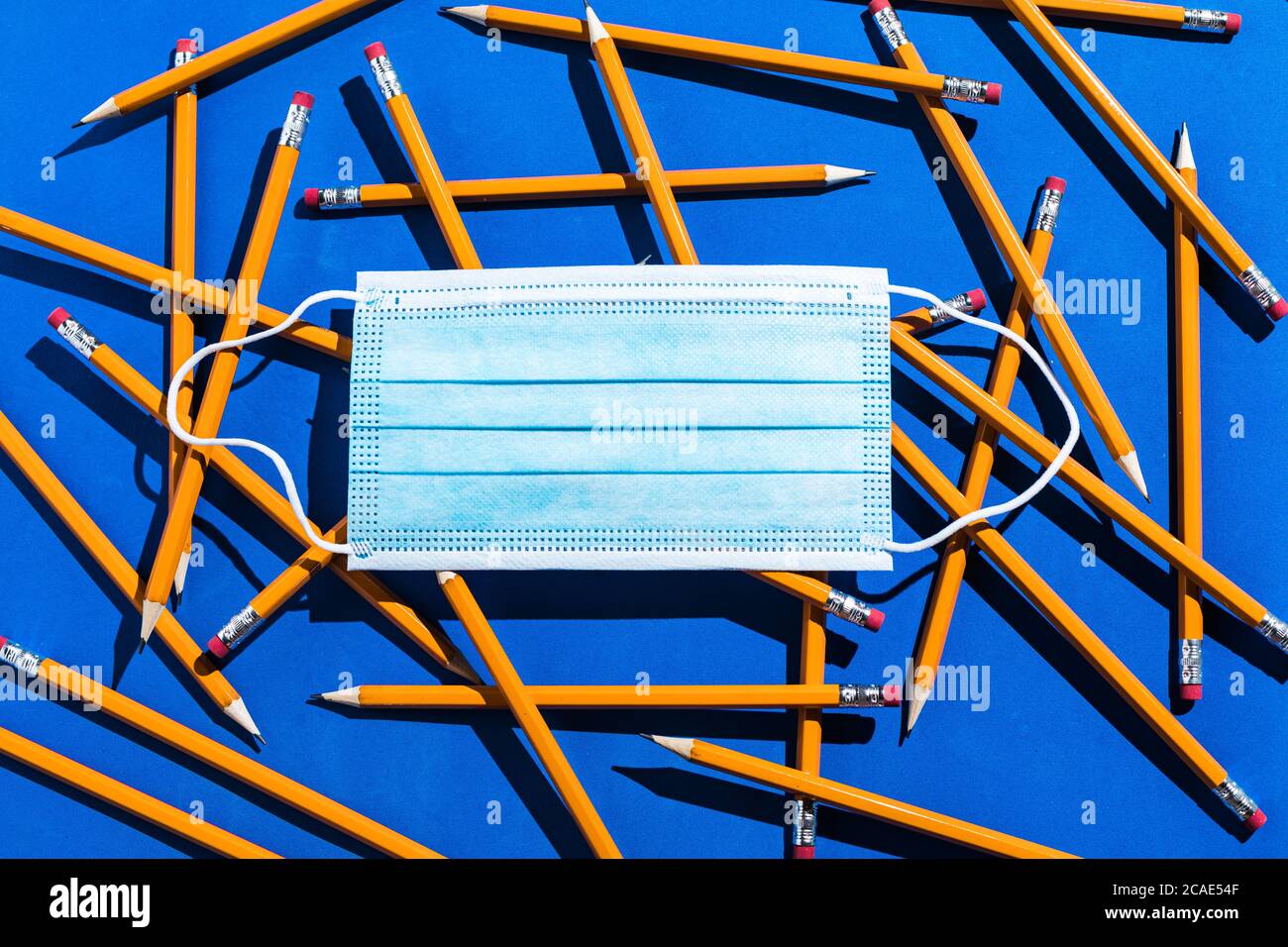 Pencils: pattern of orange pencils and surgical mask from above on blue ...