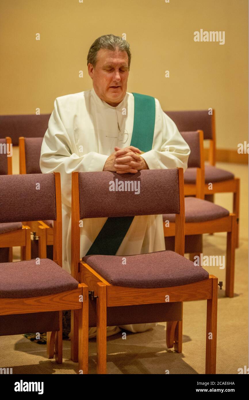 Wearing a white robe, a deacon prays on his knees in the chapel of a ...