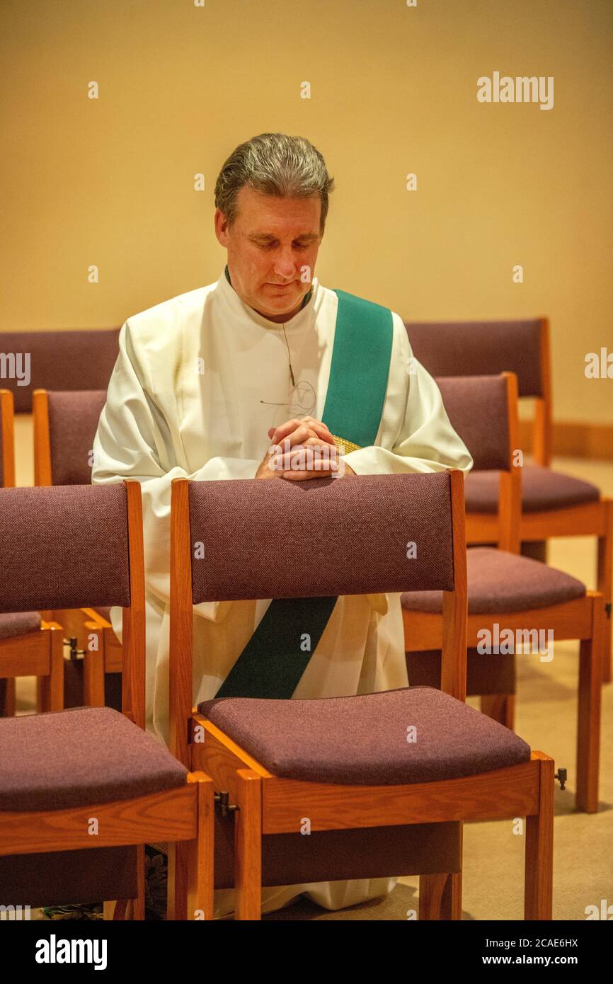 Wearing a white robe, a deacon prays on his knees in the chapel of a ...