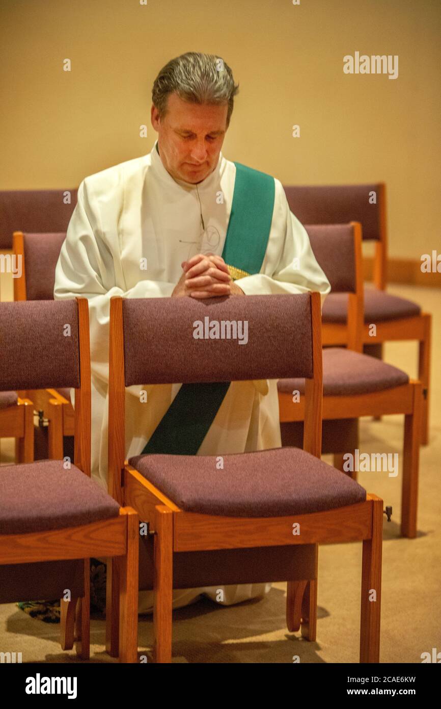 Wearing a white robe, a deacon prays on his knees in the chapel of a ...