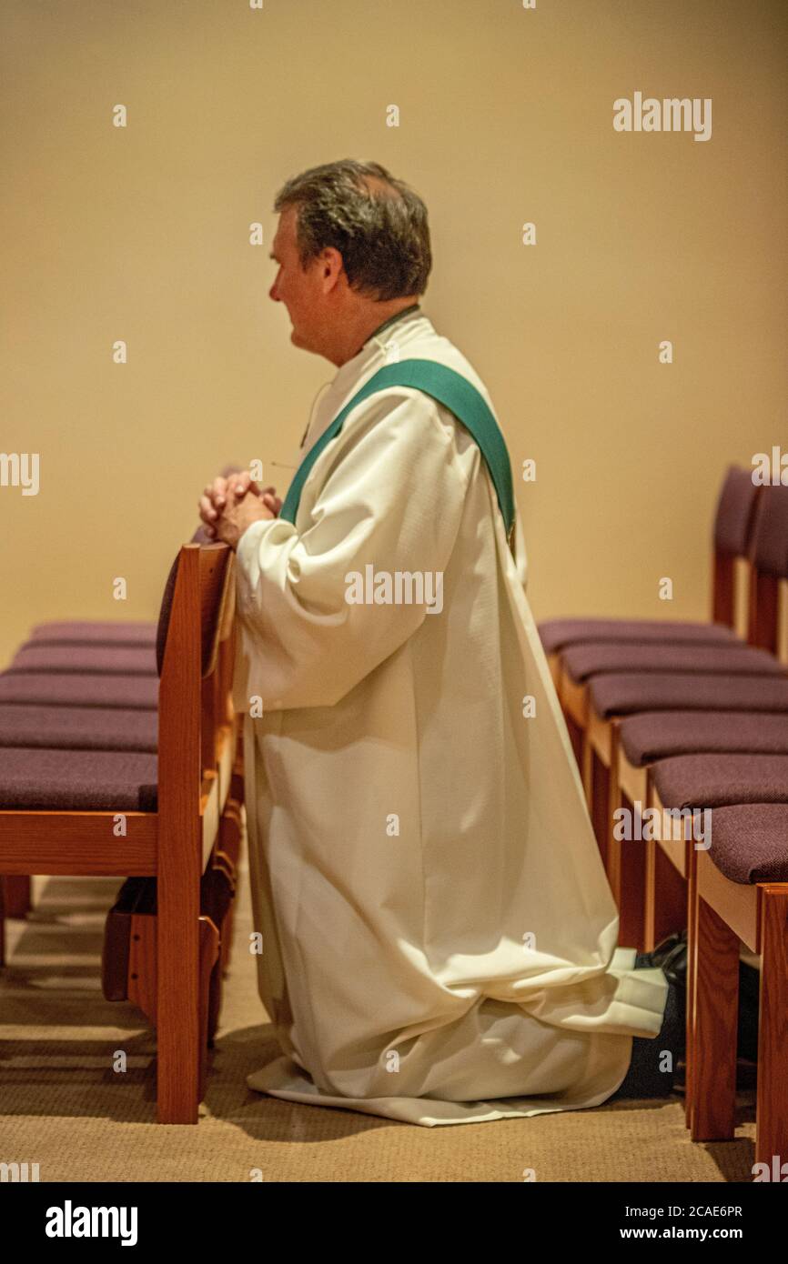 Wearing a white robe, a deacon prays on his knees in the chapel of a ...