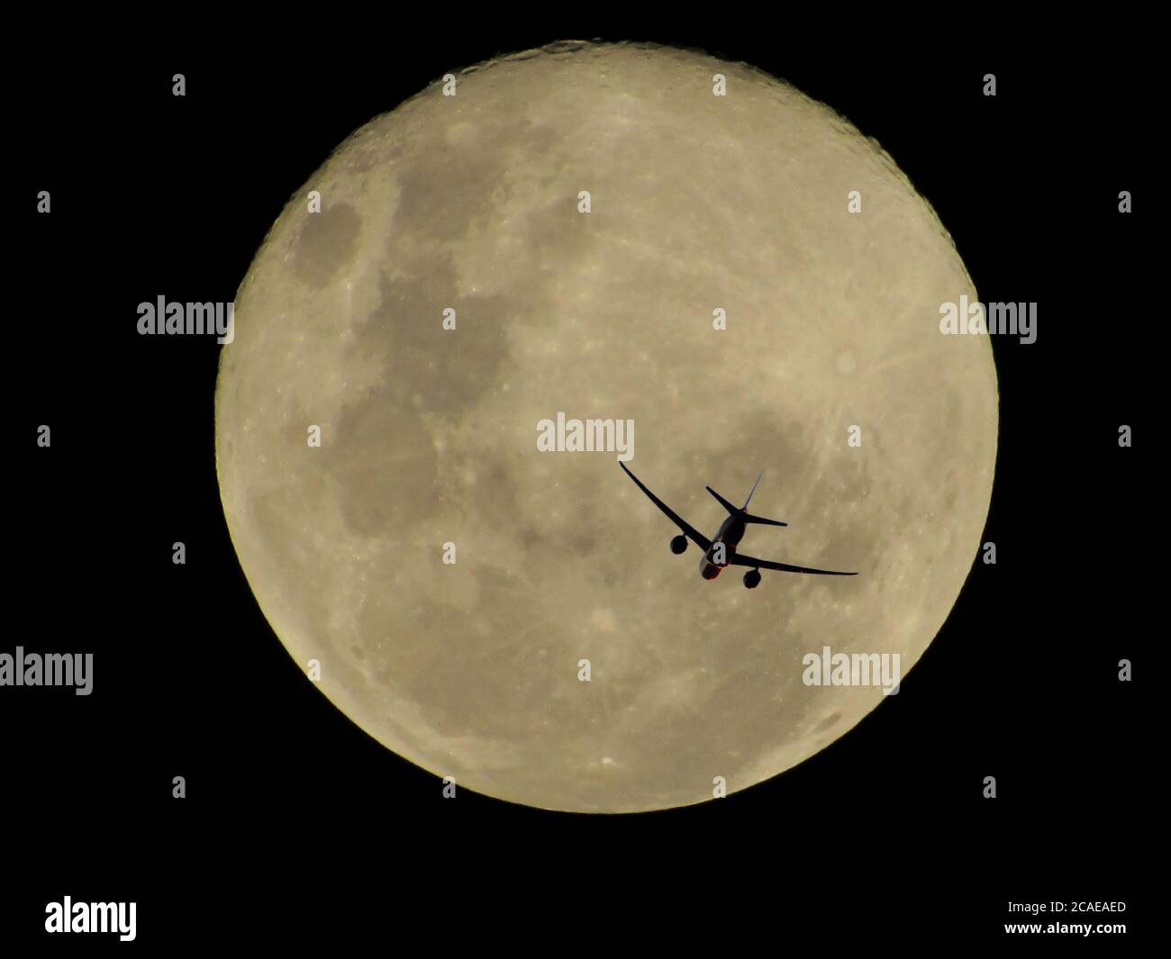 jet plane flying over the full moon that has a golden hue during a ...