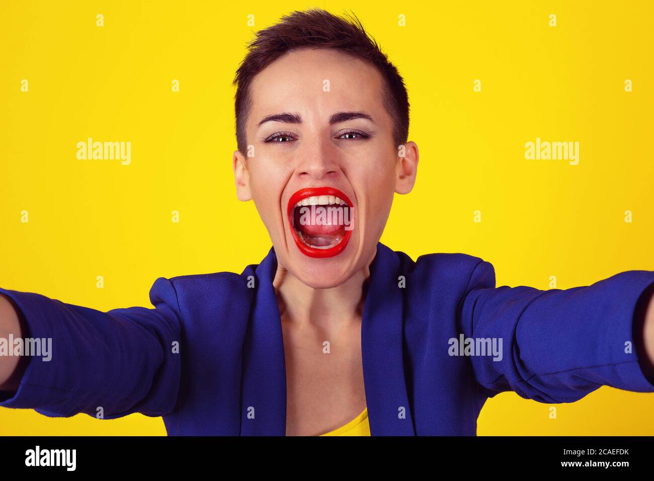 Woman screaming yelling while making selfie photo on yellow background ...