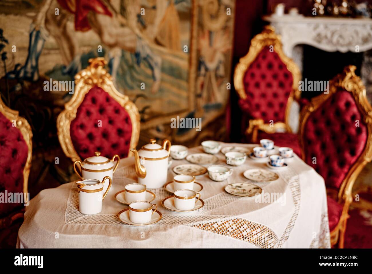 A tea set for four on a table with lace tablecloth and chairs with gold ...