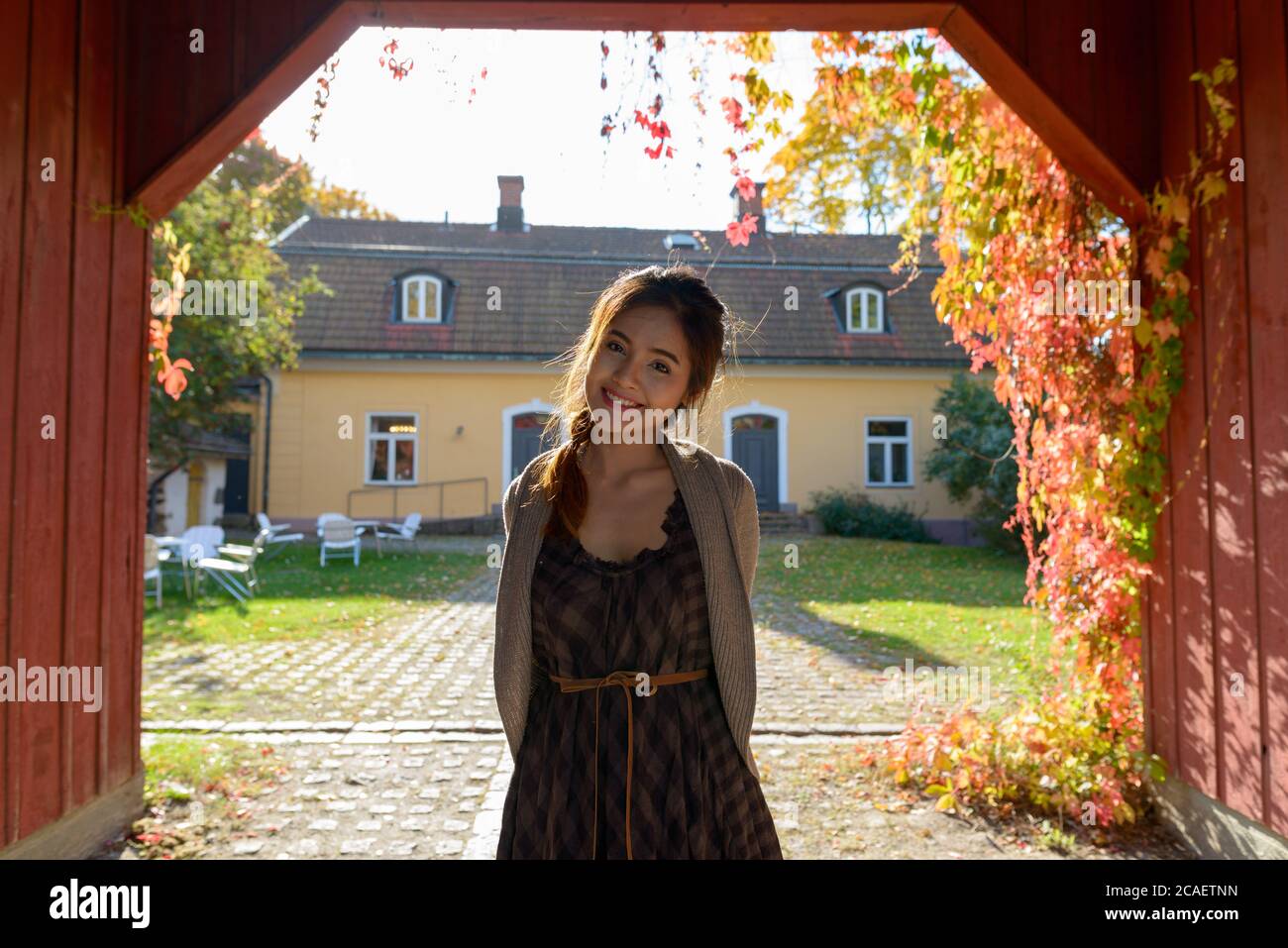 Young happy Asian woman smiling in wooden entrance of elegant suburban ...