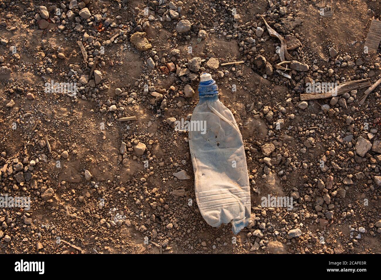 an old plastic bottle lies on ground, yellow sand and stones on ...