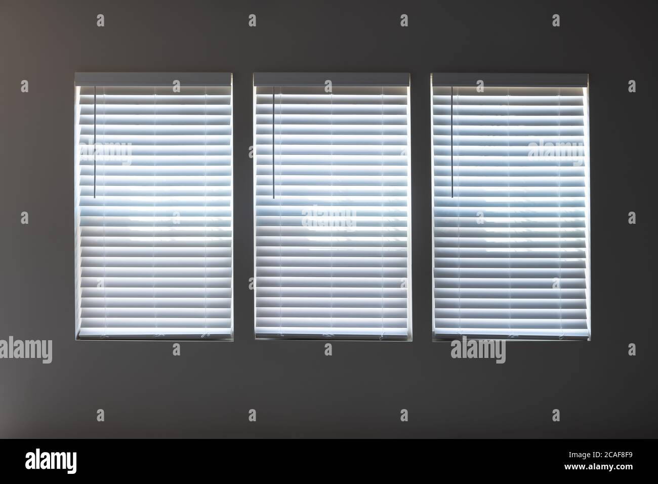 Three windows with closed modern white wood faux window blinds as ...