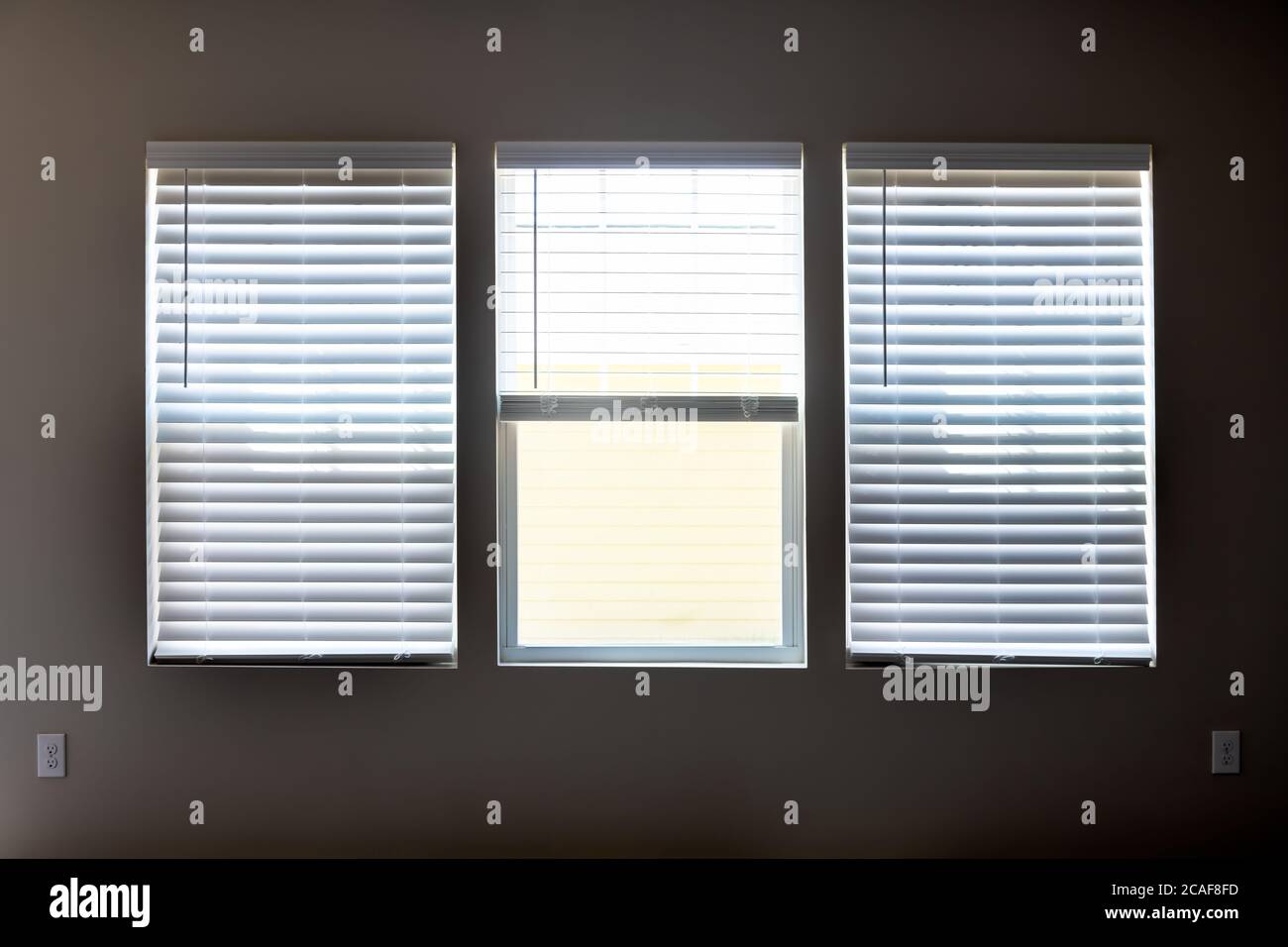 Three windows with closed modern white wood faux window blinds as ...
