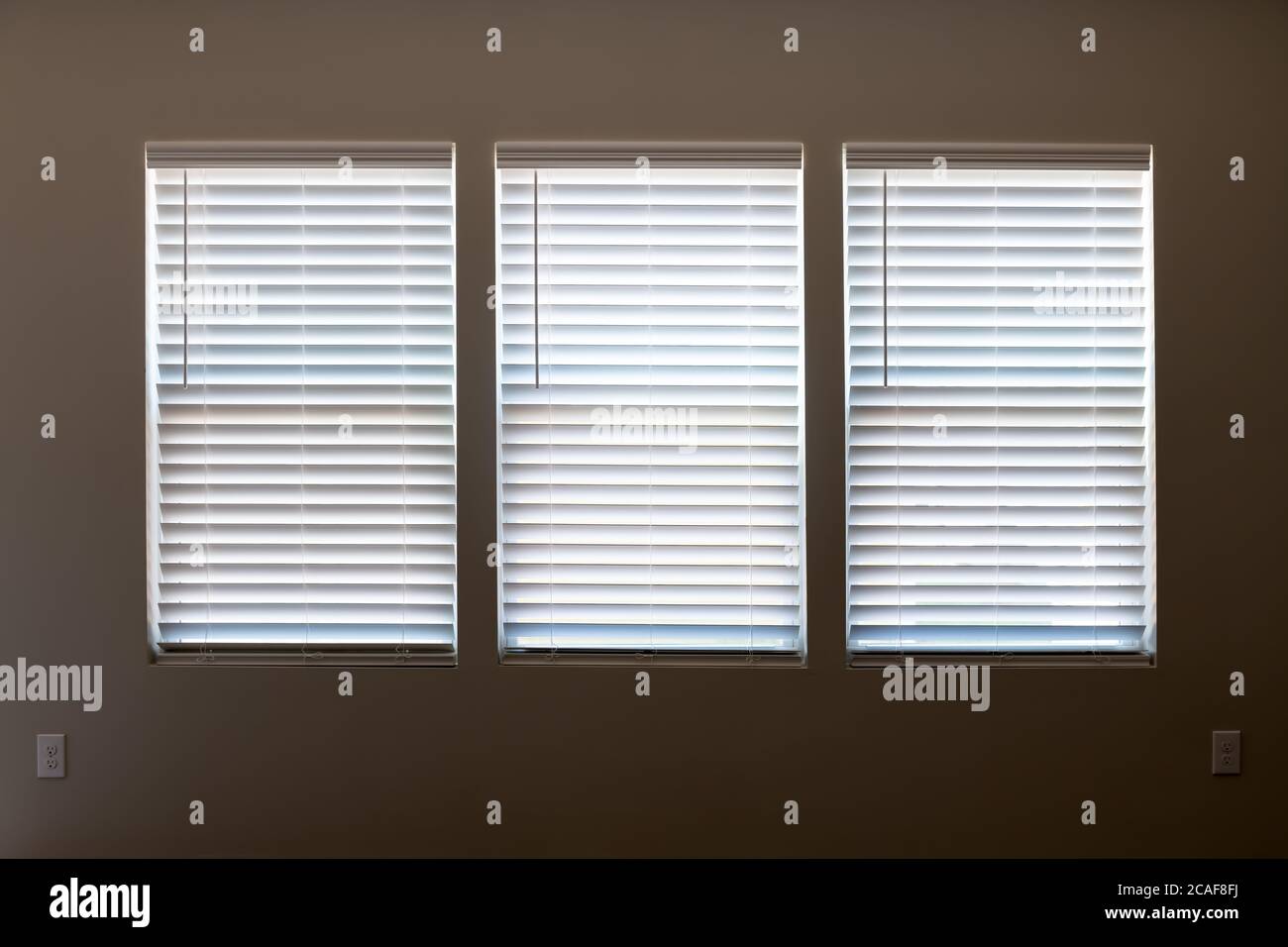 Three windows with closed modern white wood faux window blinds as ...