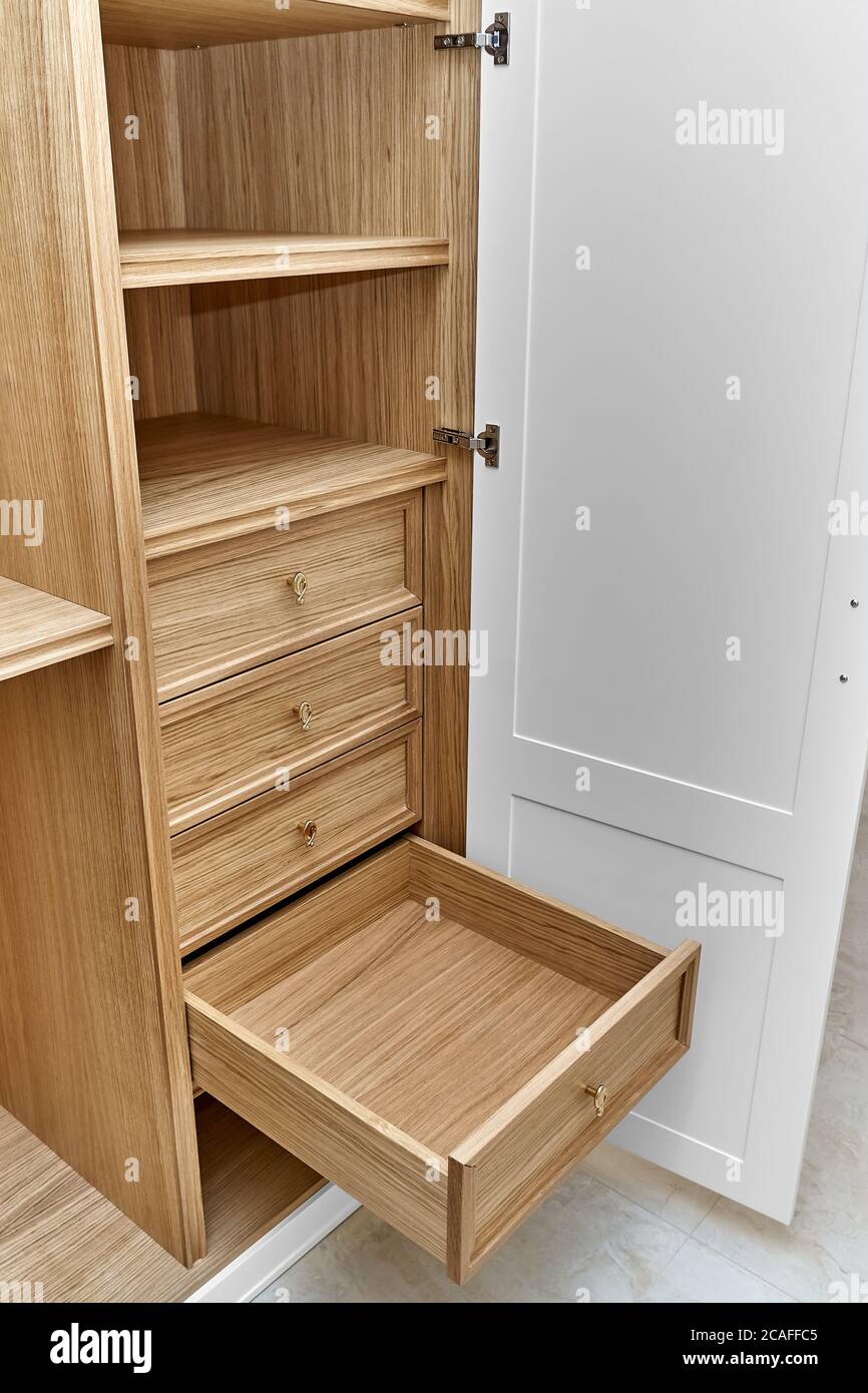 Opened white wardrobe with wooden drawers and shelves. Wooden filling ...