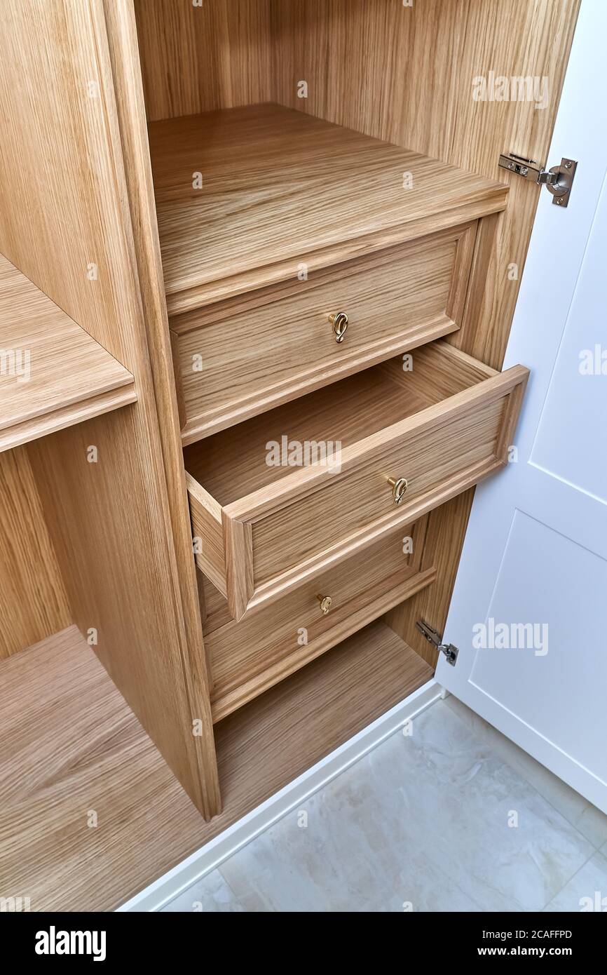 Opened white wardrobe with wooden drawers and shelves. Wooden filling ...