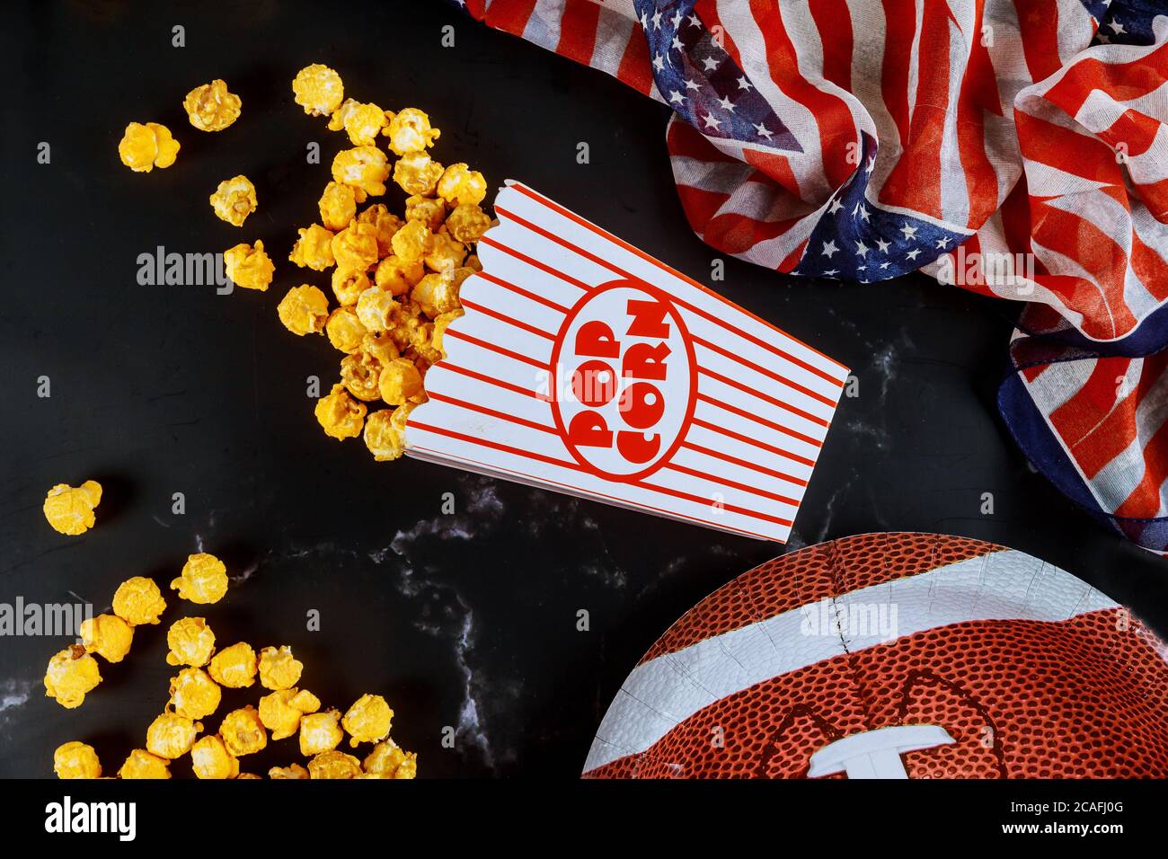 Yellow popcorn in striped boxes spilled on black background with ...