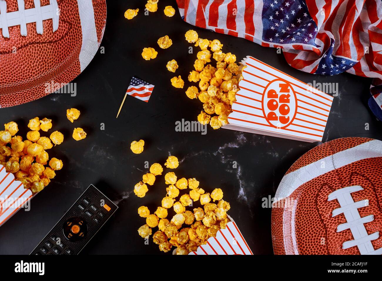 Yellow popcorn in striped boxes spilled on black background with remote ...