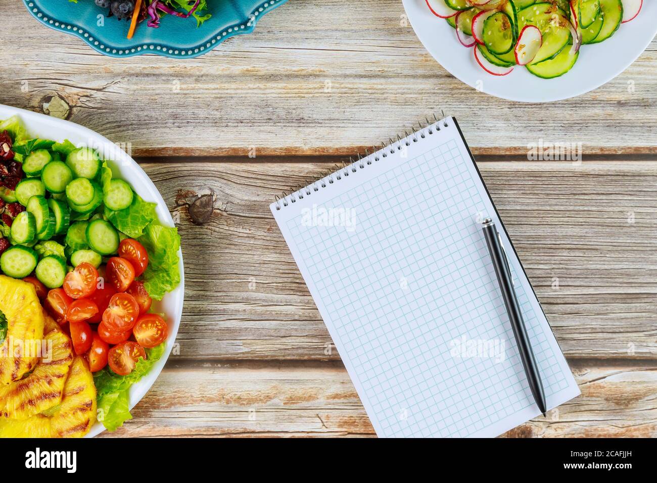 Notebook and pen for writing recipe with healthy salads on wooden table ...