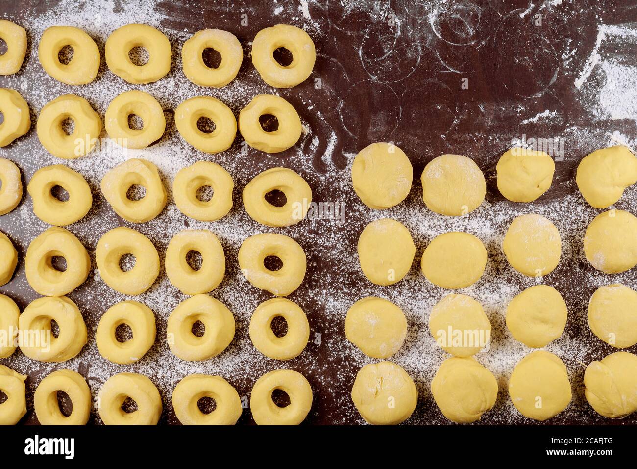 Raw round sweet donuts and munchkins on table with flour before frying ...