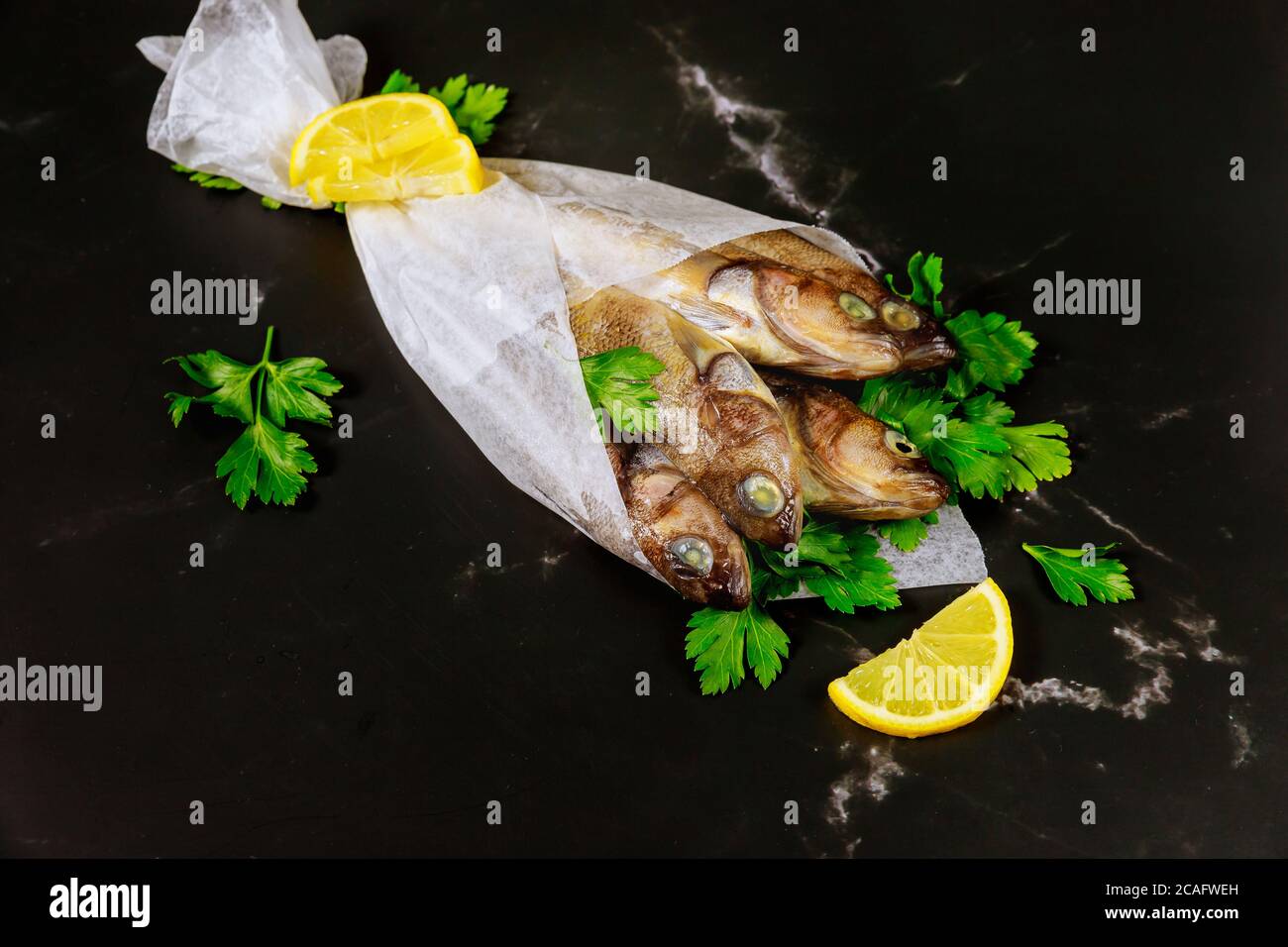Raw whole fish with parsley and lemon wrapped in parchment paper on ...