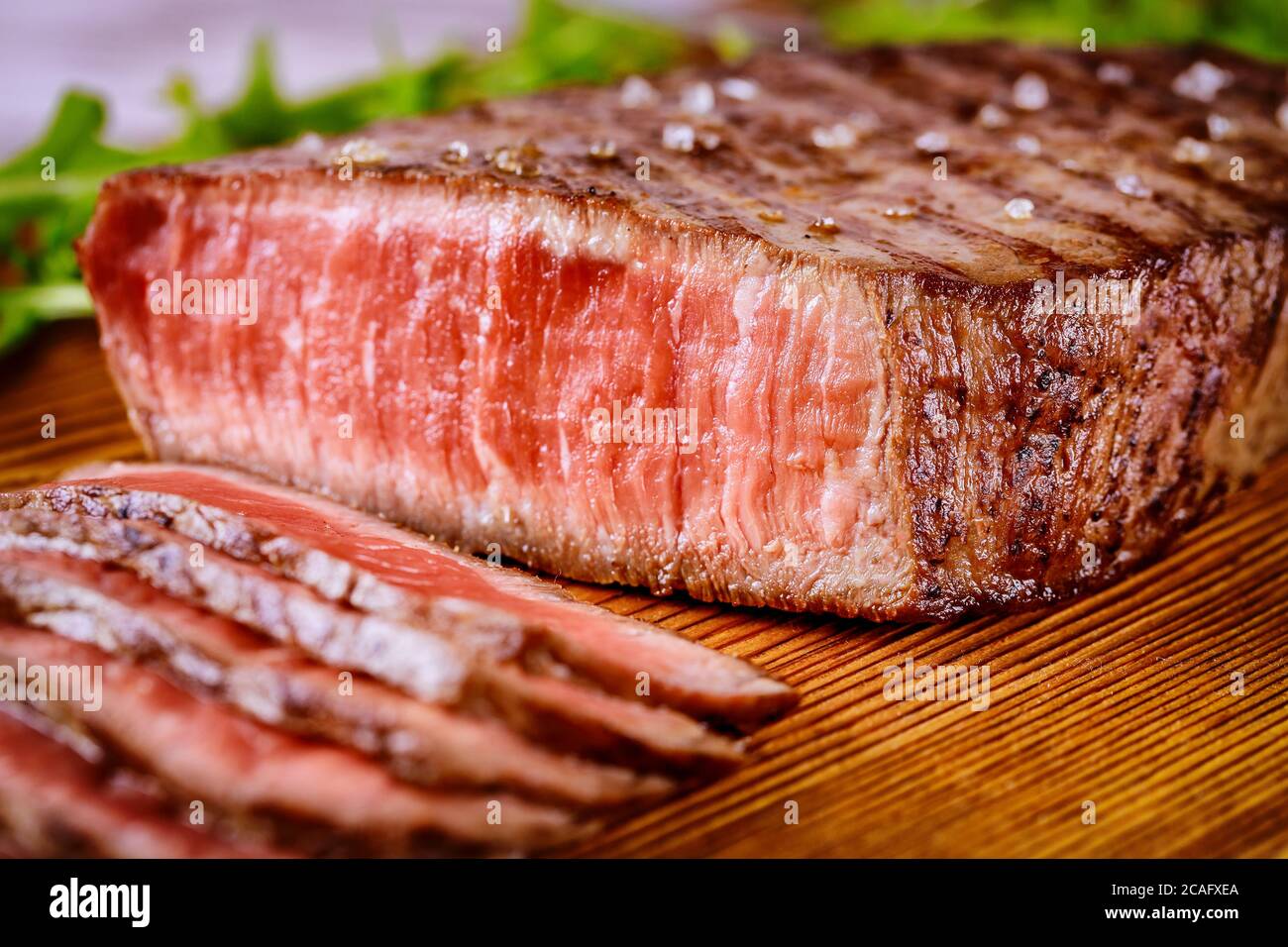 Sliced grilled rare beef steak served with arugula on wooden board ...