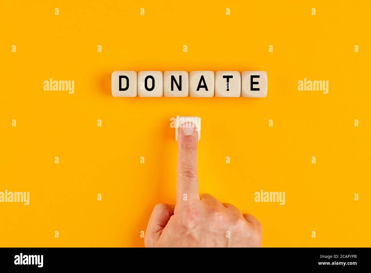 The word donate written on wooden cubes with a male hand pressing the ...