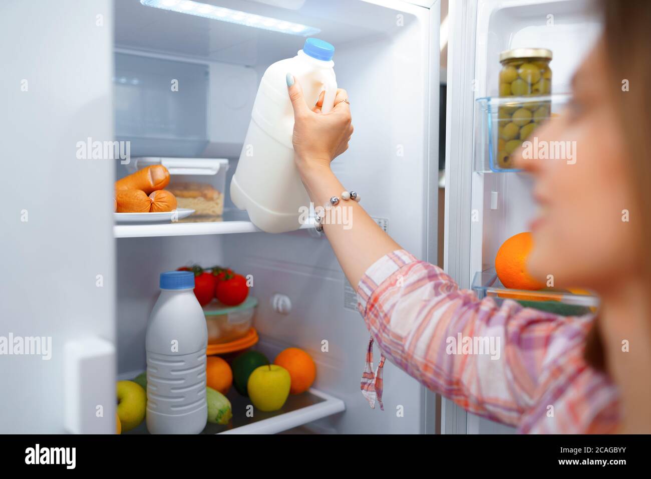 Portrait of a young blonde woman taking food from her fridge Stock ...